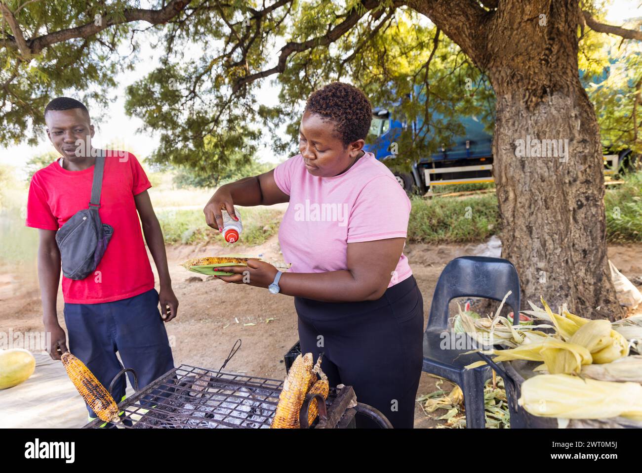 african woman street vendor selling grilled corn to a man client on a ...