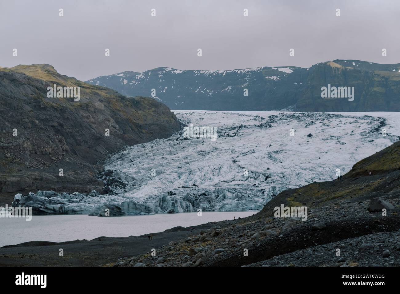Cascade of glacial ice slides down contrast green grey mountainside ...