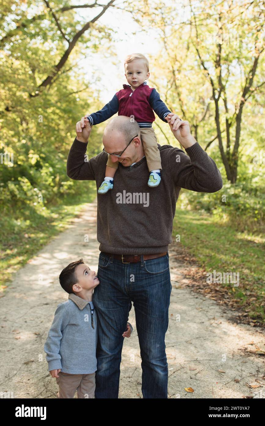 Dad carrying child on shoulders while another child is hugging his leg ...