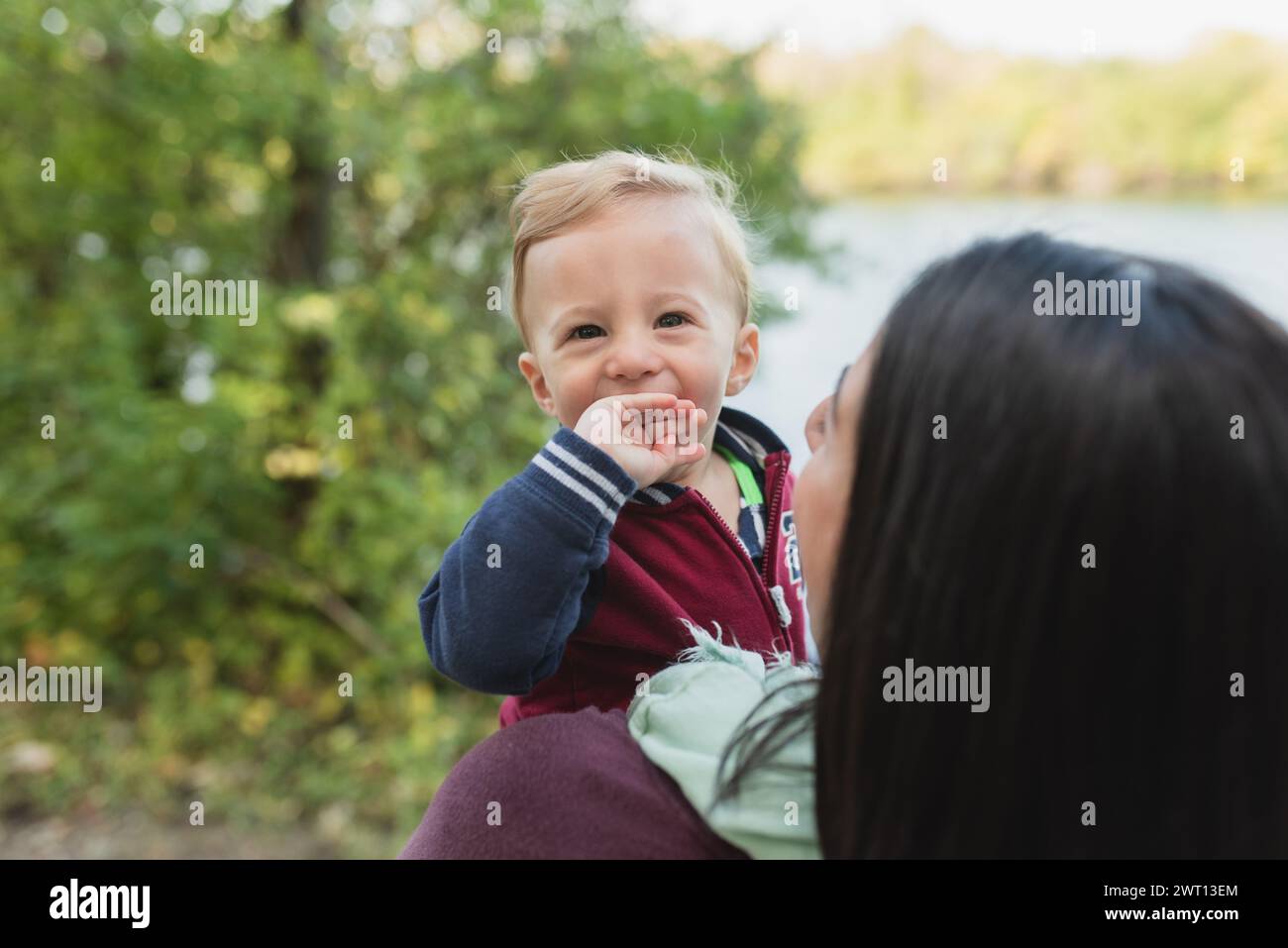 Laughing child covering his mouth while looking over mom's shoulder ...