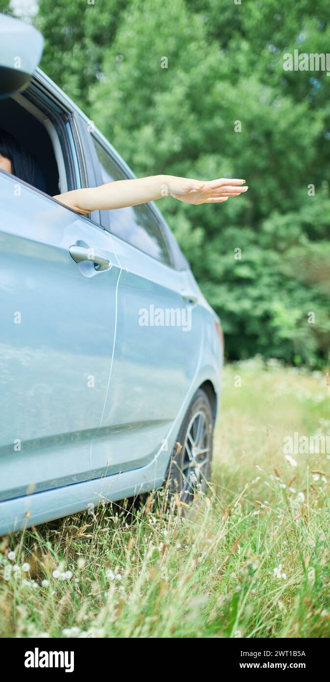 Woman arm reaching out from the side window of a blue car, set against ...