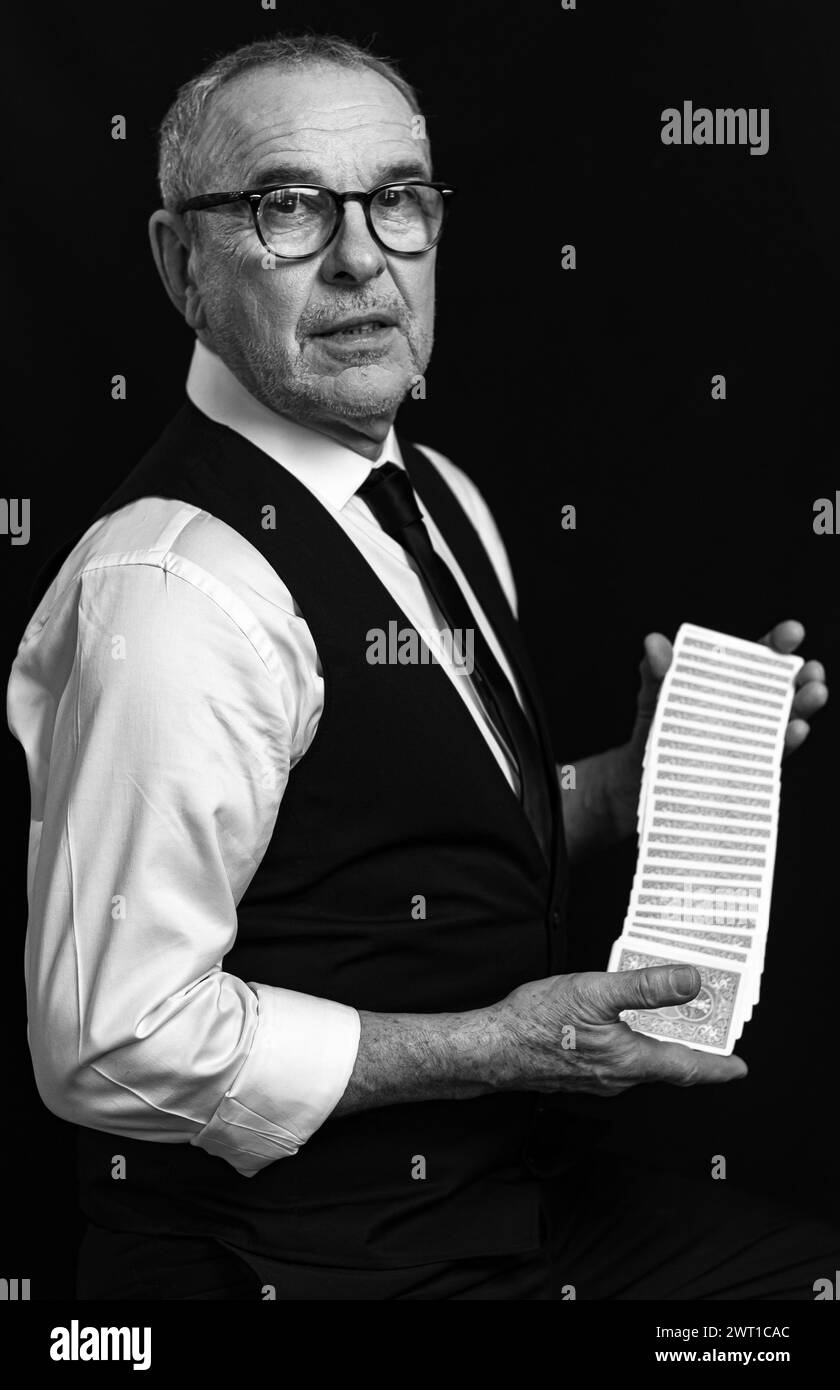 A magician manipulates playing cards to perform a magic trick. Dressed ...