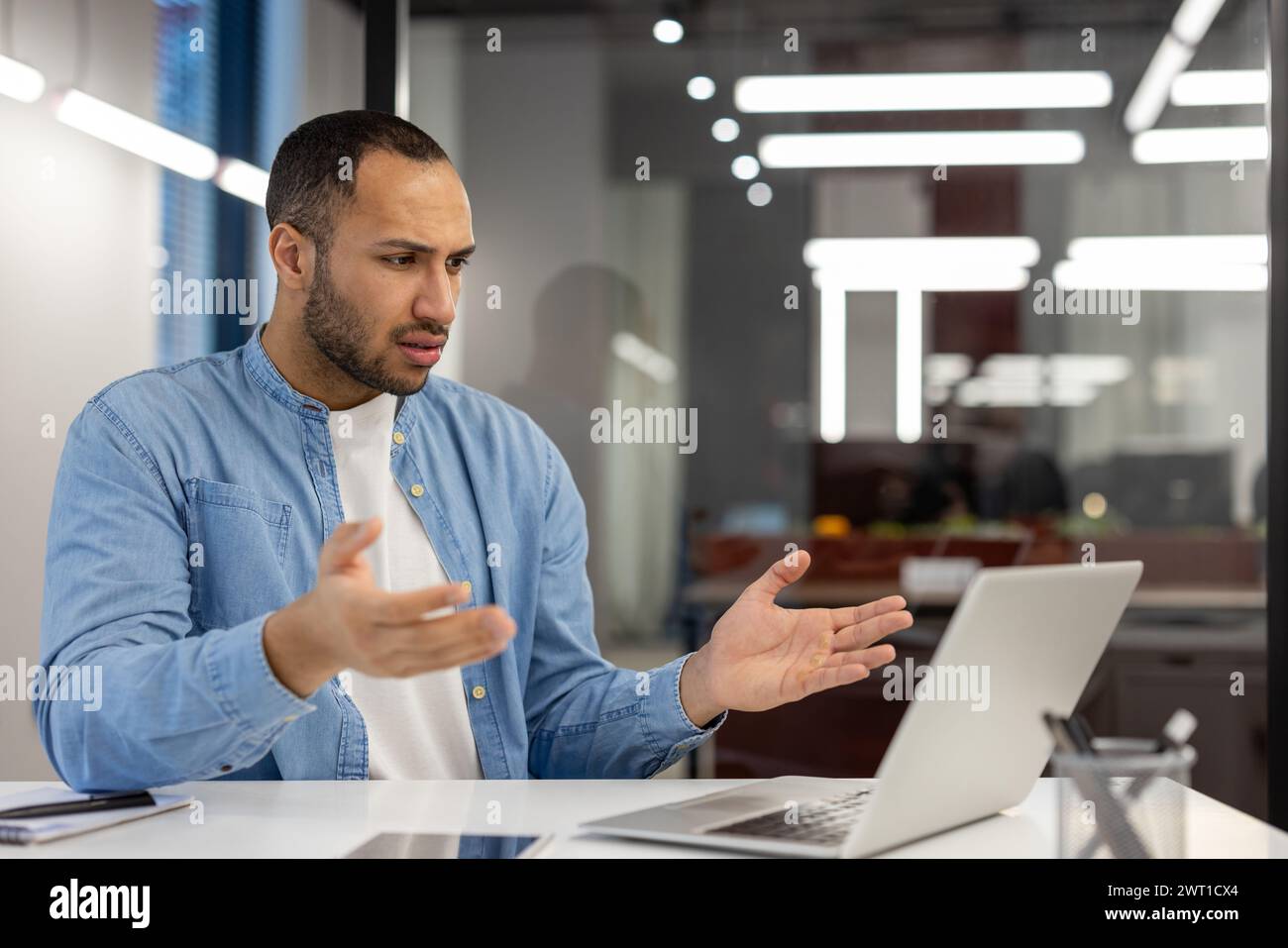 Shocked and worried young hispanic man sits at a desk in a modern ...