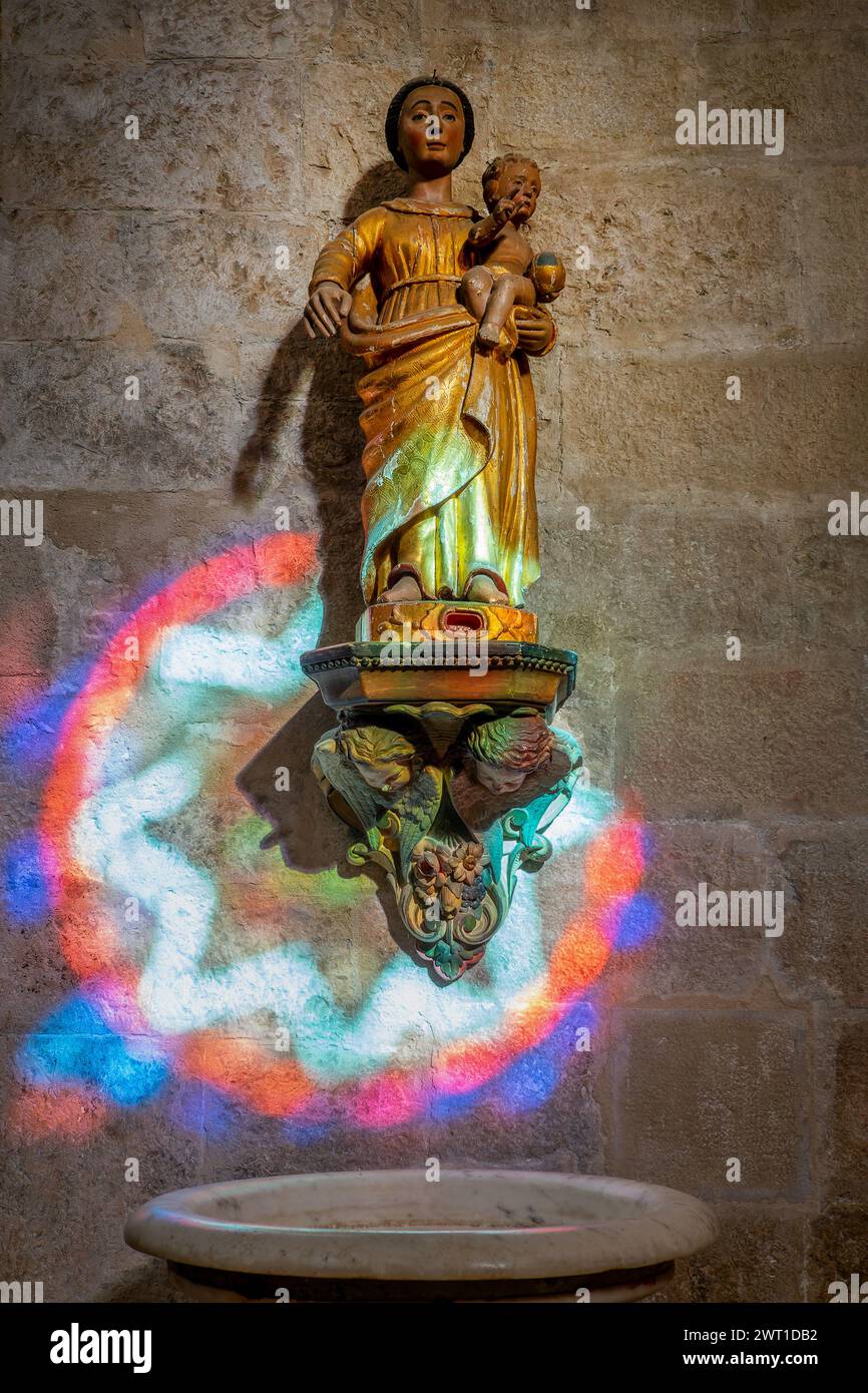 Virgin and child statue illuminated by the colorful light of a stained ...