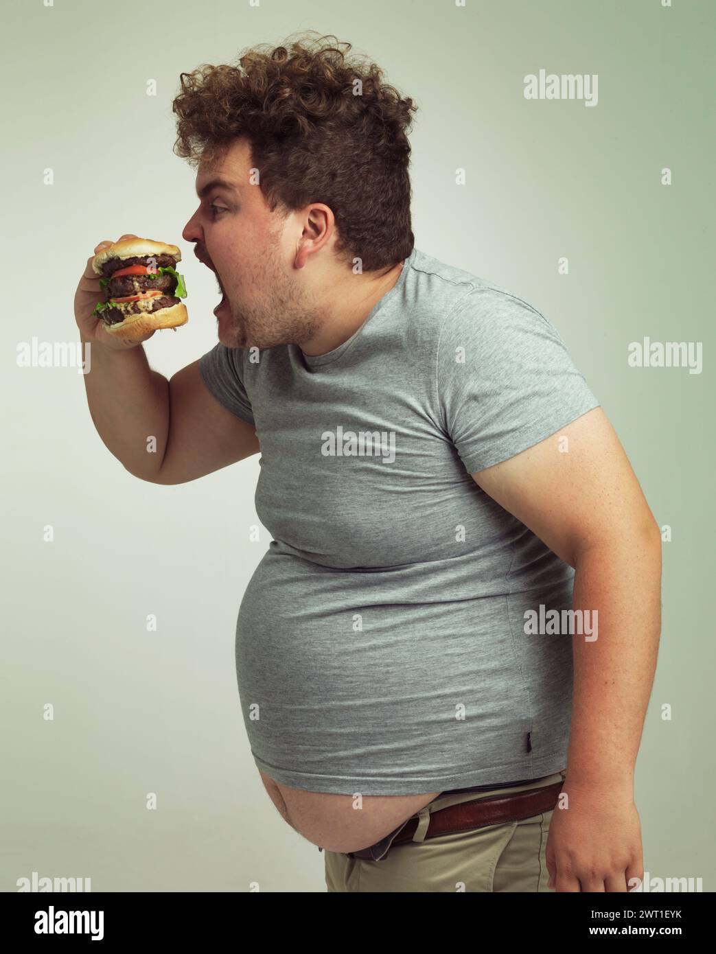 Obesity, weight gain and fast food for man in studio with burger for ...