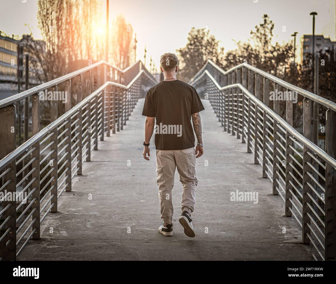 A man is walking across a bridge that spans over a street. The man ...