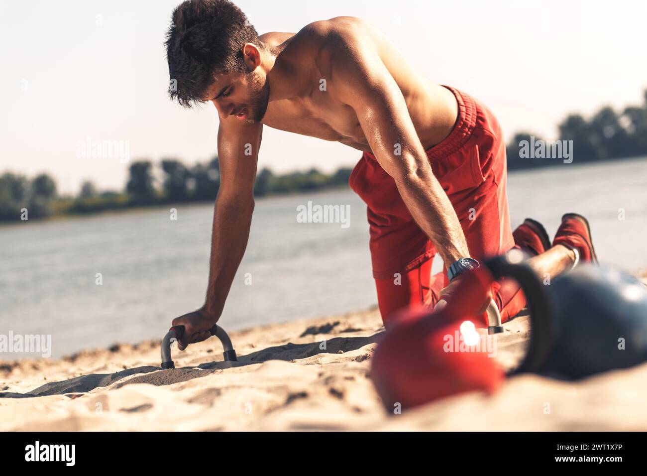 Man doing fitness workout at a beach using kettlebell for push ups ...