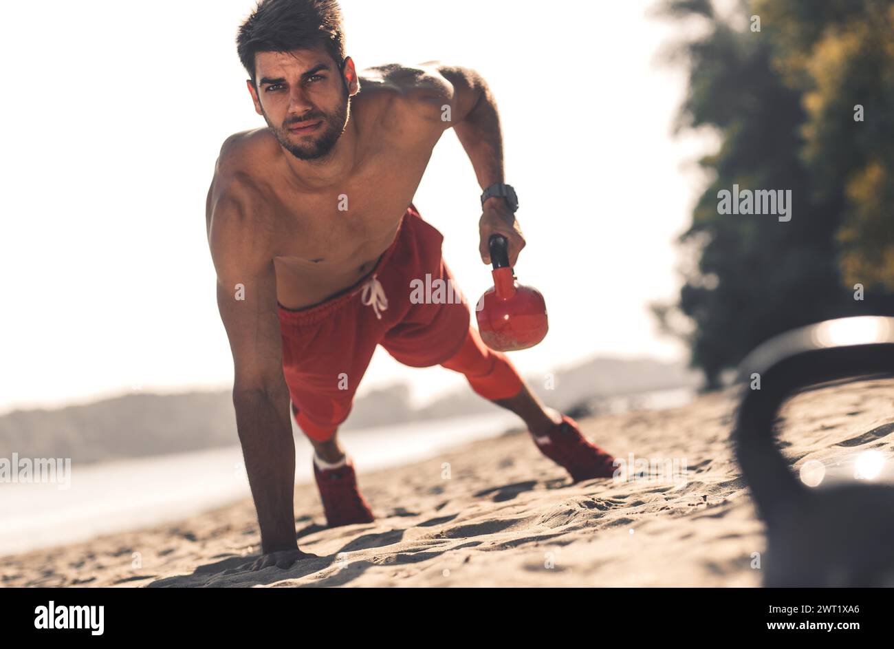 Man doing fitness workout at a beach using kettlebell for push ups ...