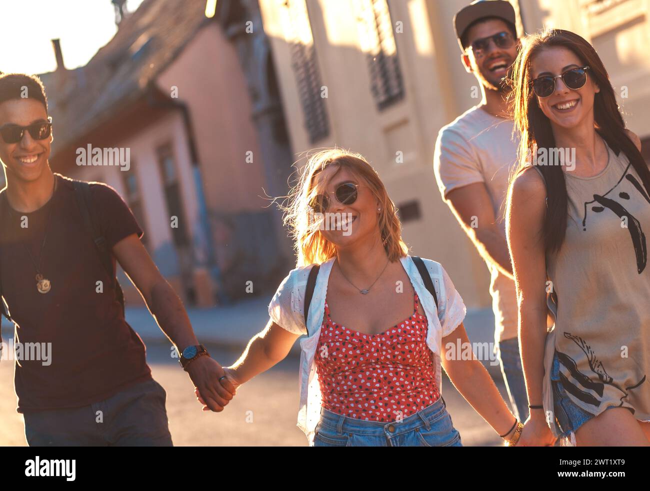 Group of friends walking and laughing at the city street at sunset ...