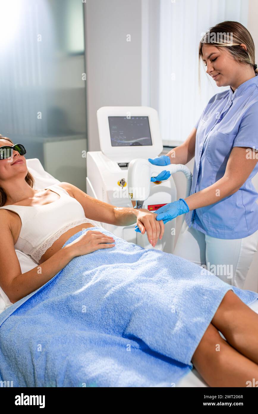 Woman in a beauty salon removes hair from her arm with laser epilation ...