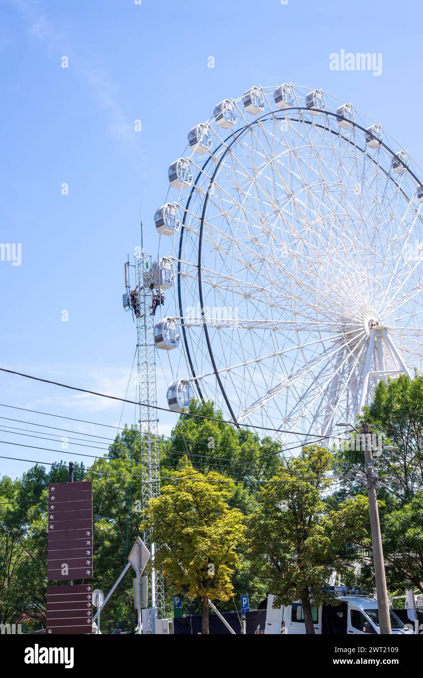 Workers on a communication tower by a ferris wheel in white color ...