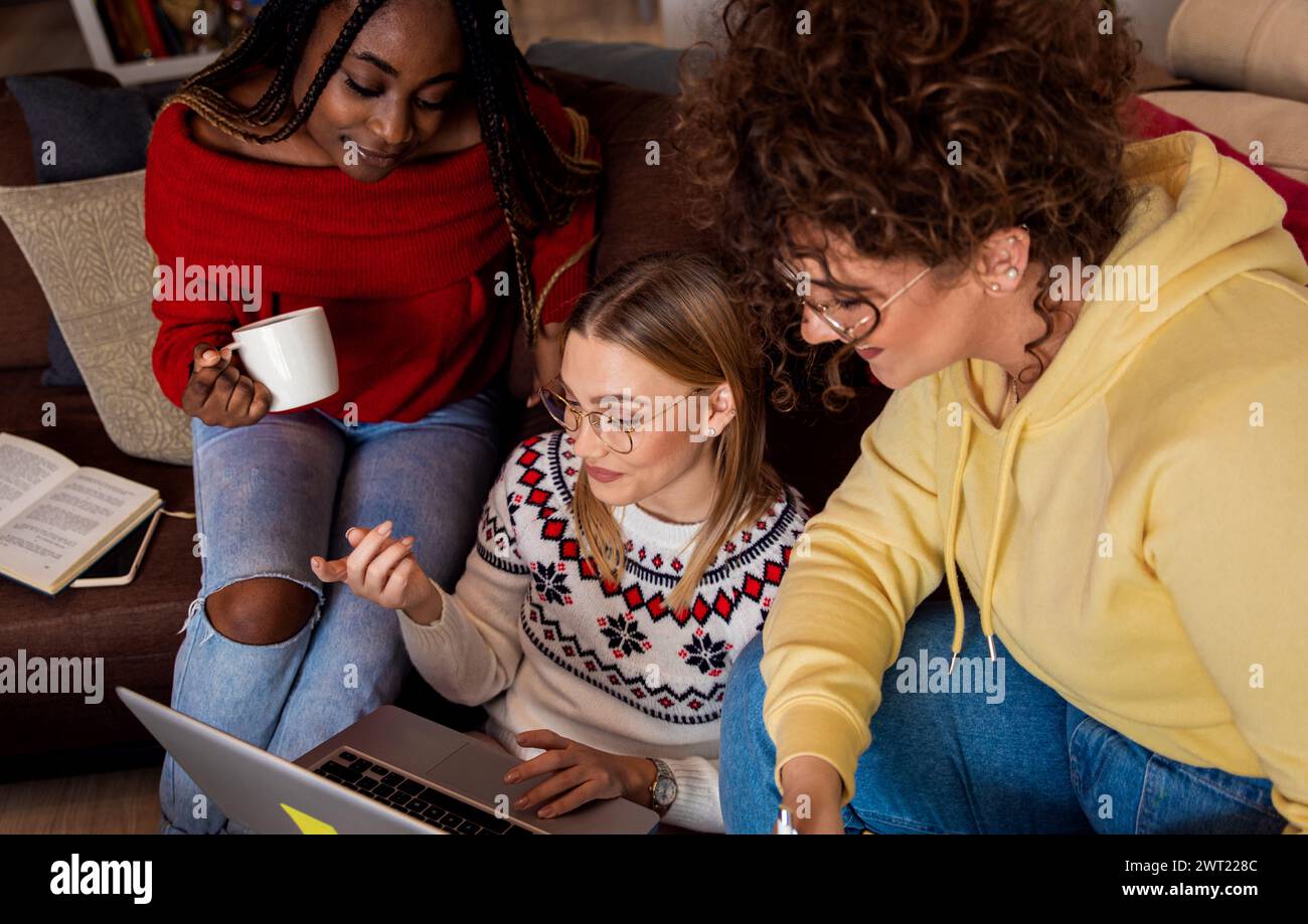 Diverse group female students learning at home using laptop and books ...