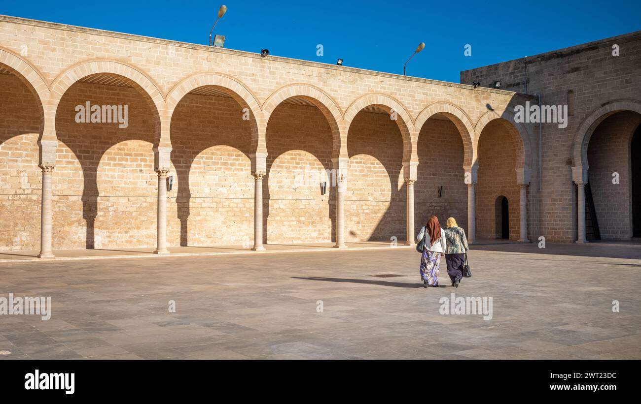 Two muslim women wearing hijab walk hand-in-hand across the sahn, or ...