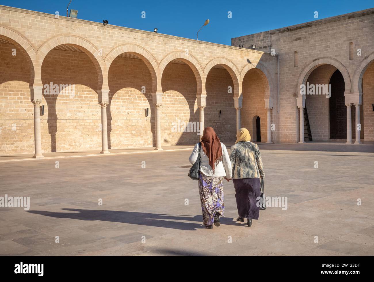 Two muslim women wearing hijab walk hand-in-hand across the sahn, or ...