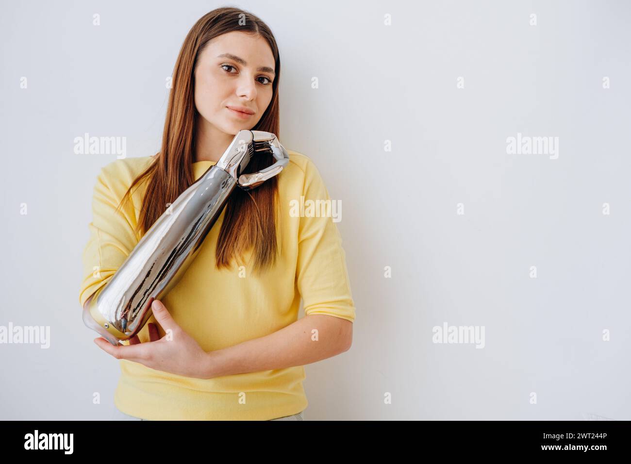 A young woman, deep in thought, cradles her robotic arm, reflecting the ...