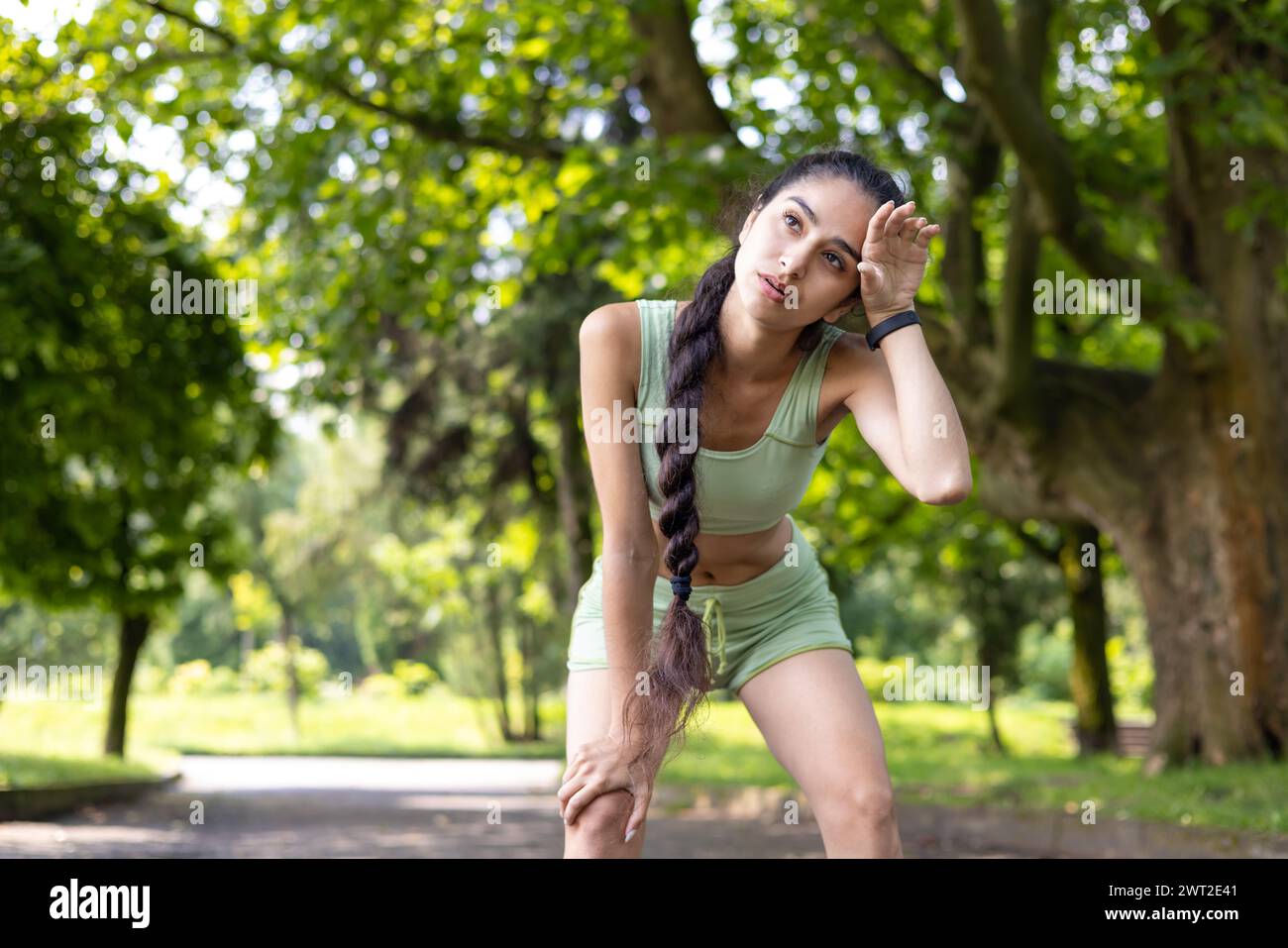 A tired Indian young woman is standing in the park hunched over ...