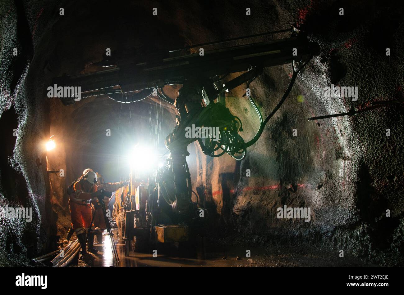Two miners working in a dimly lit underground tunnel with mining ...