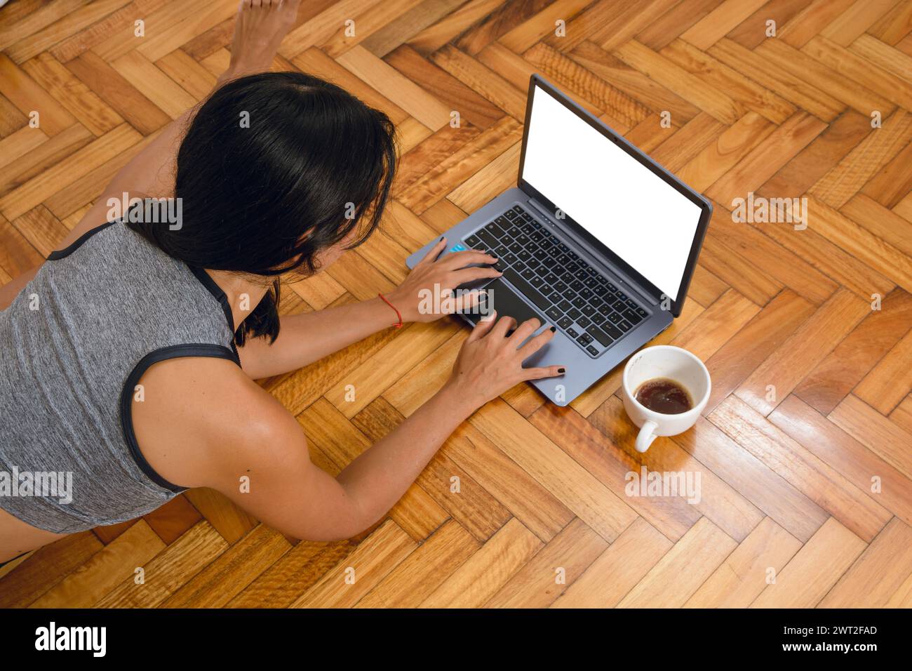 top view of unrecognizable young brunette woman on floor with cup of coffee, lying down writing ...