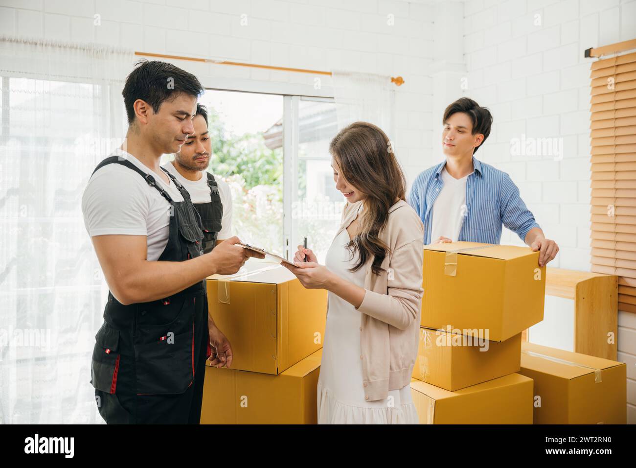 Couple inspects checklist before signing moving papers. Worker carries a box. Professional ...