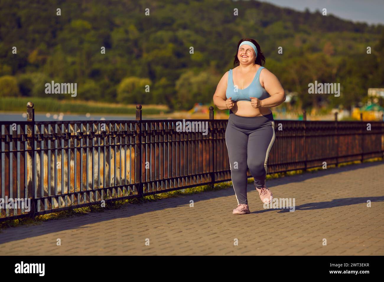Overweight happy smiling fat woman running in the summer city park ...