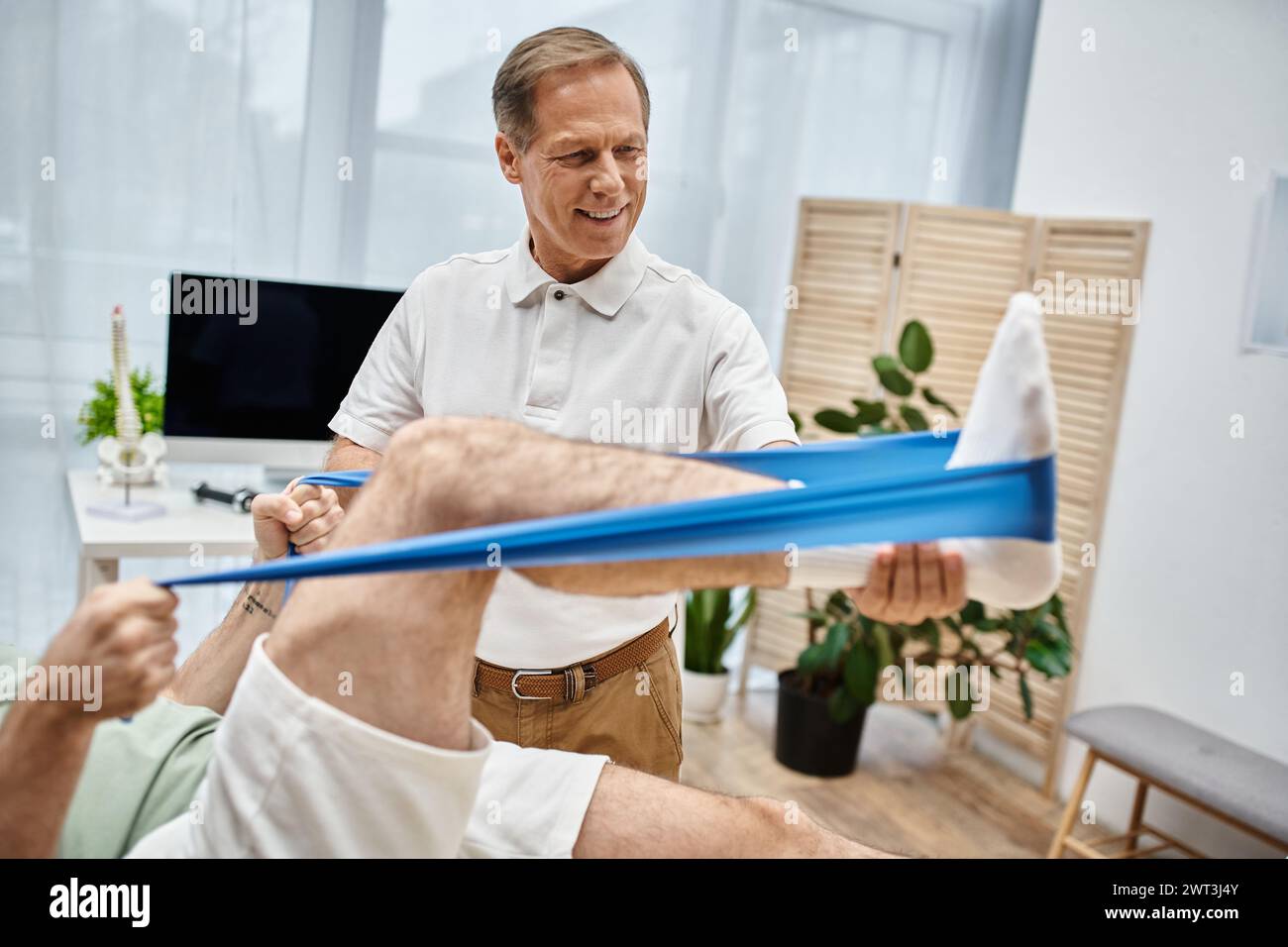 cheerful handsome doctor helping his patient to stretch with resistance ...