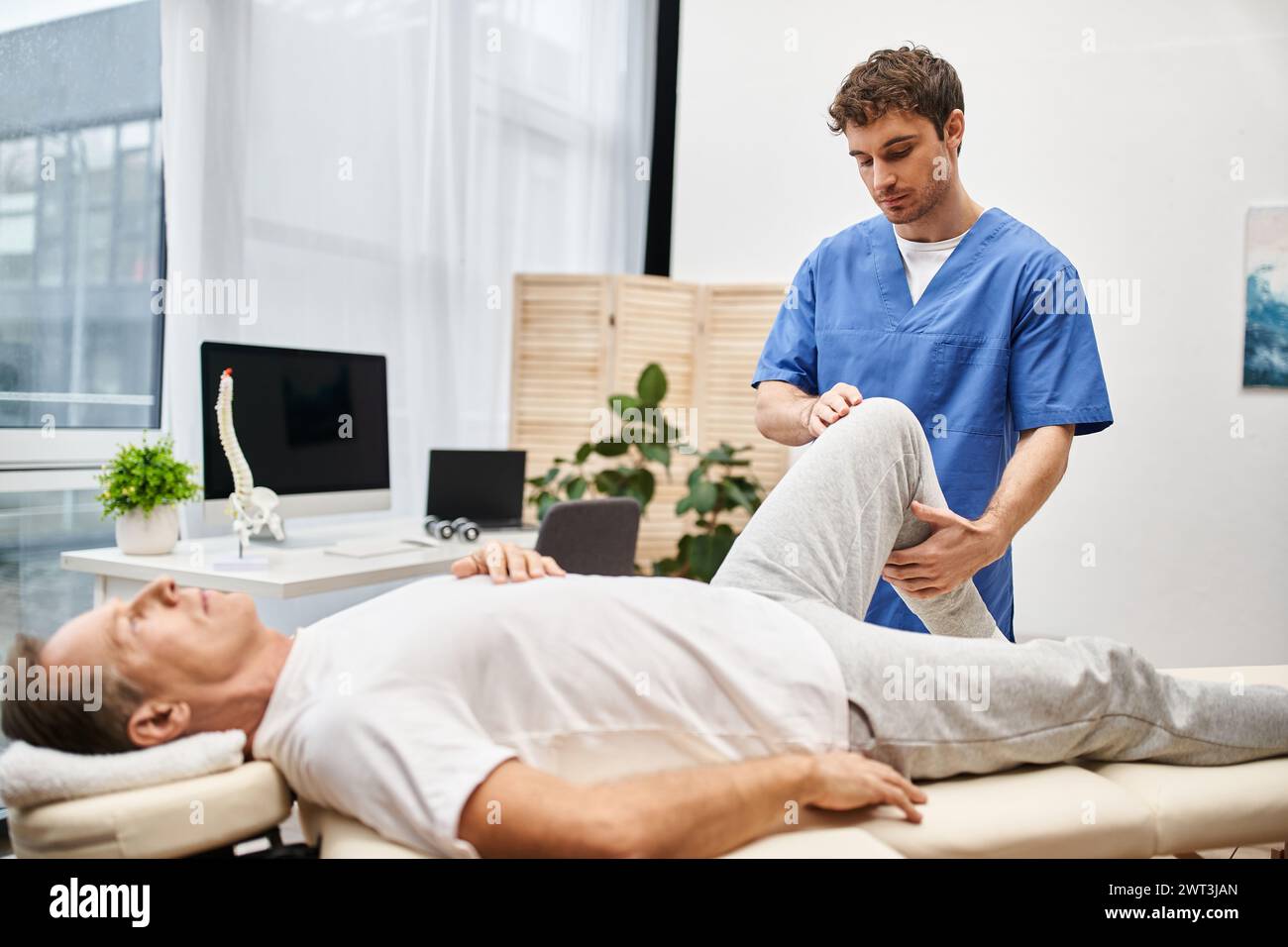 good looking doctor in blue robe helping his mature patient to stretch ...