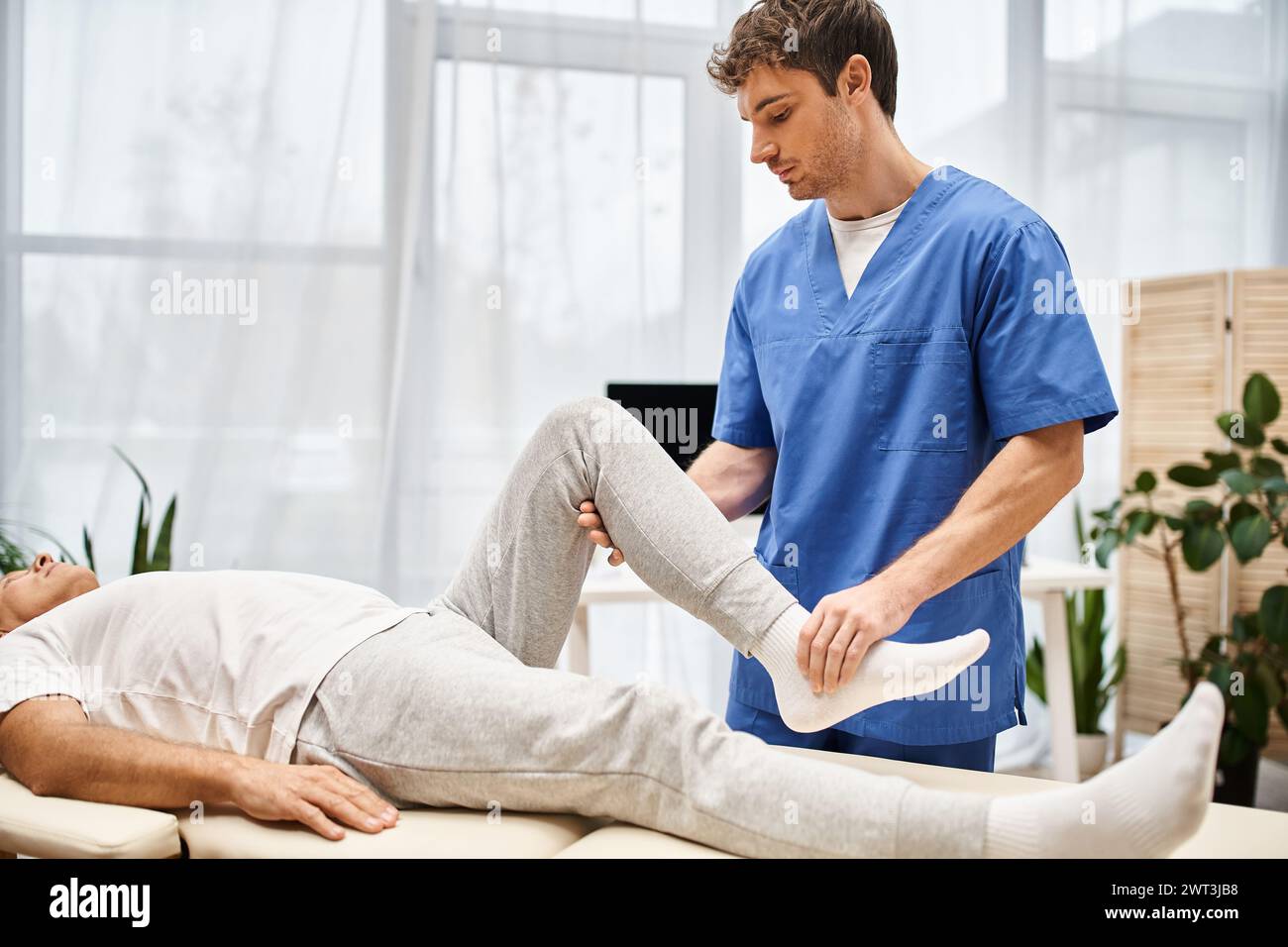 attractive devoted doctor rehabilitating muscles of his mature patient ...