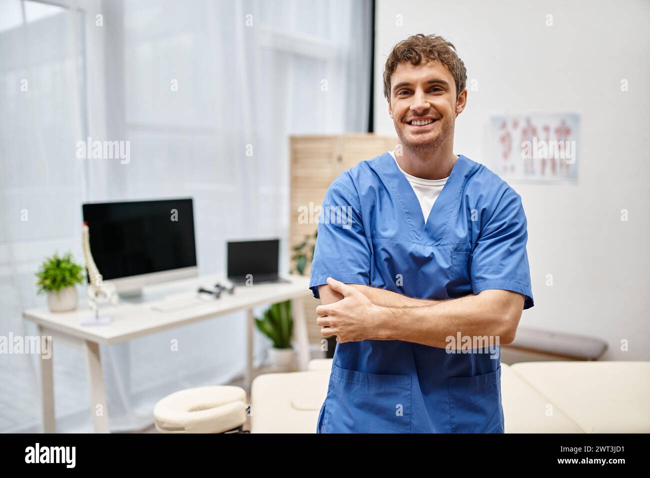 joyful dedicated rehabilitologist in blue uniform posing in hospital ...