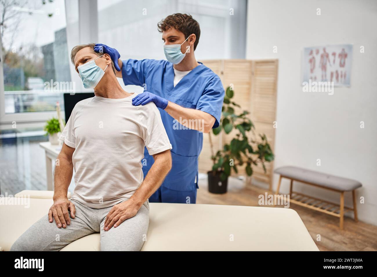 devoted doctor with mask and gloves helping his patient to stretch his ...
