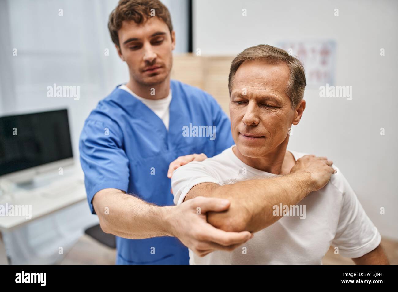 good looking patient in casual attire stretching his muscles with help ...