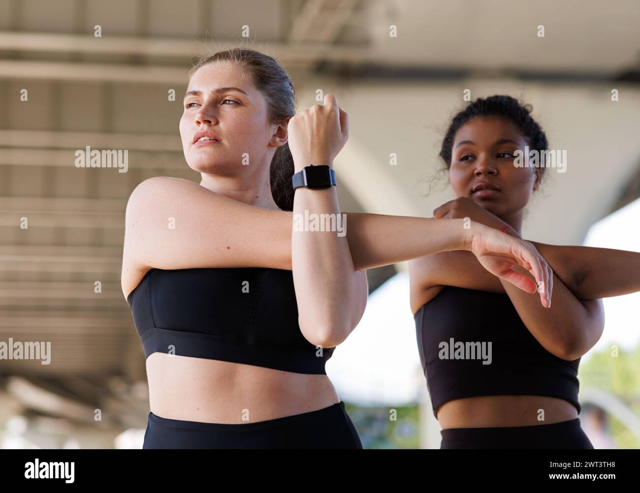 Two females stretch their hands while practicing under a bridge. Young ...