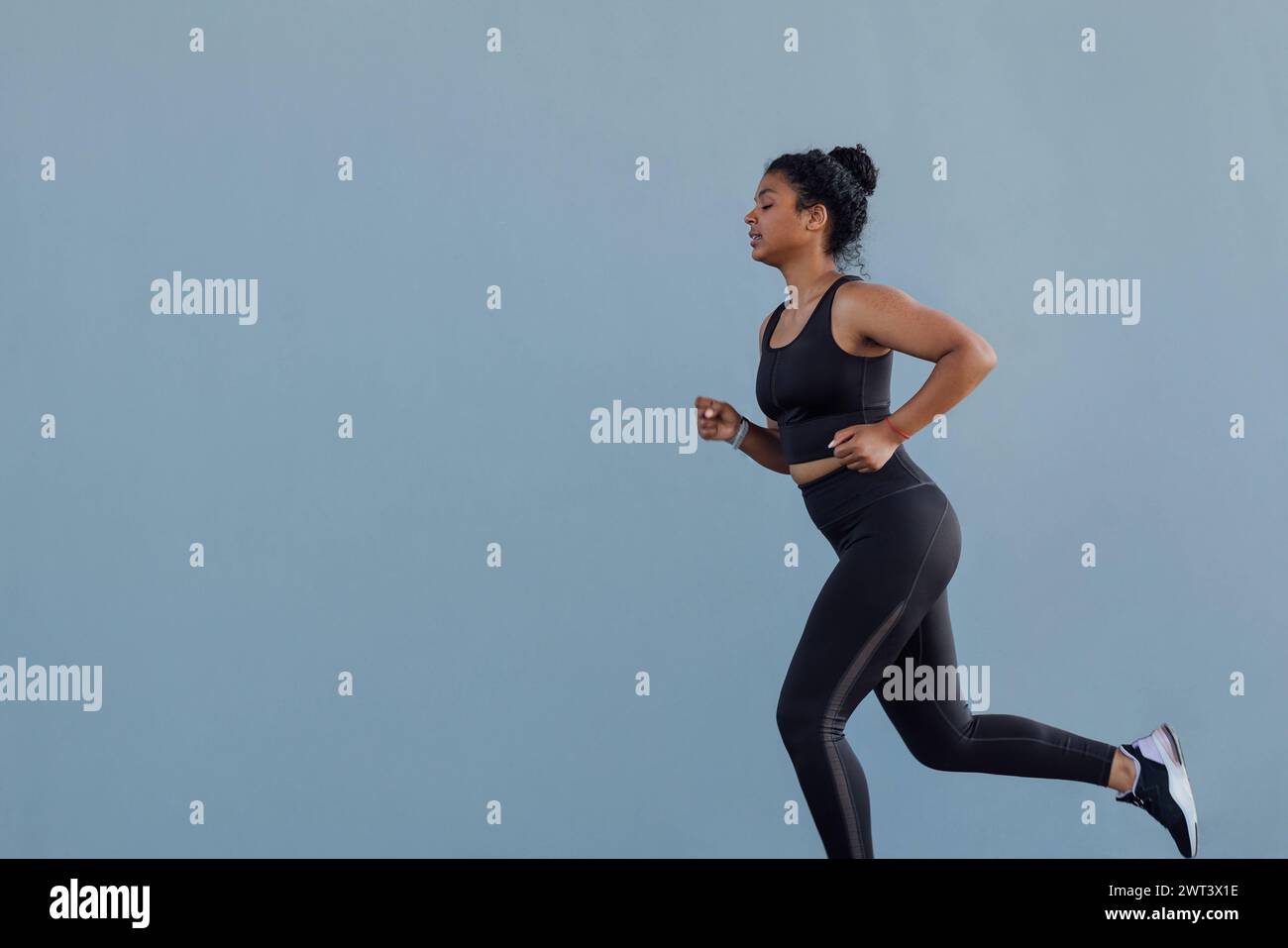 Side view of young female running at a grey wall. Woman in black ...