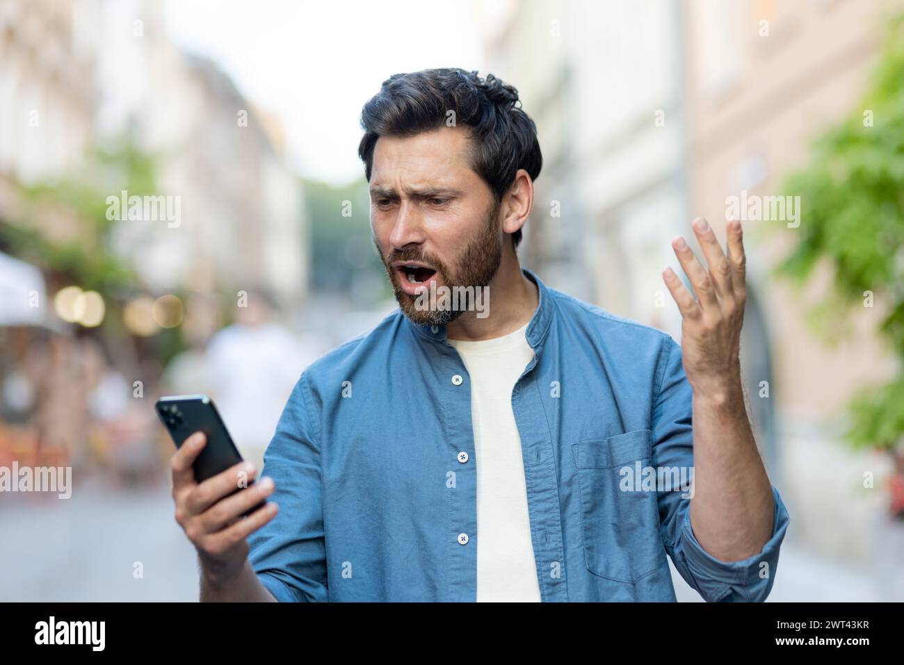 An angry young man in casual clothes stands on a city street and looks ...