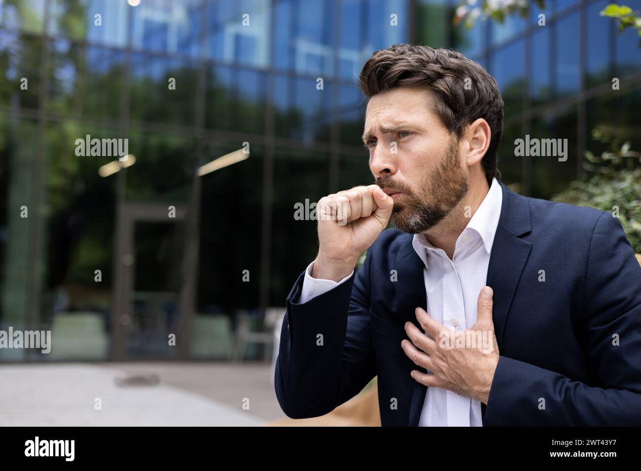 A young male businessman suffers from asthma and allergies. He sits outside an office building ...