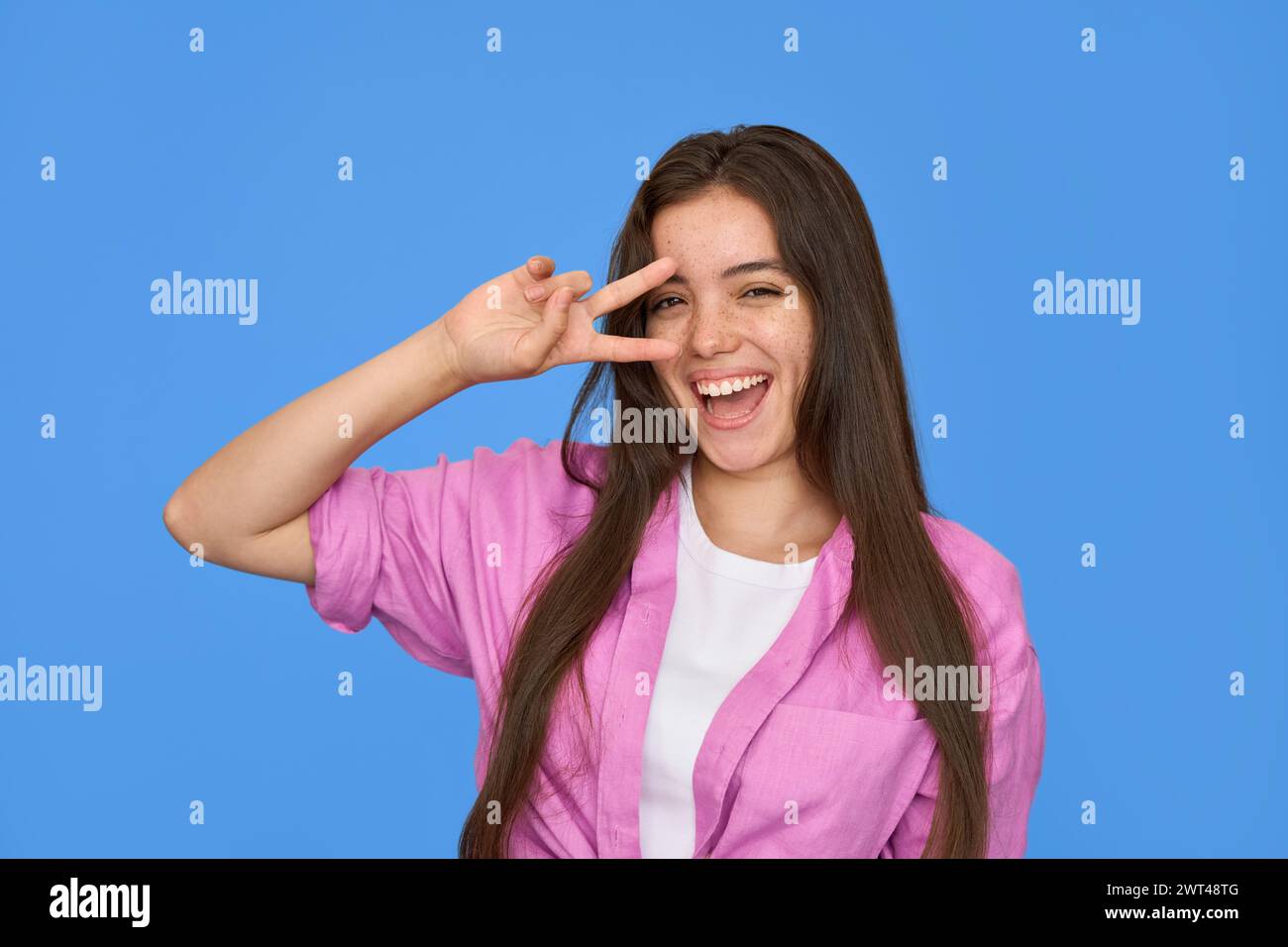 Happy gen z Latin girl showing peace sign over face isolated on blue ...