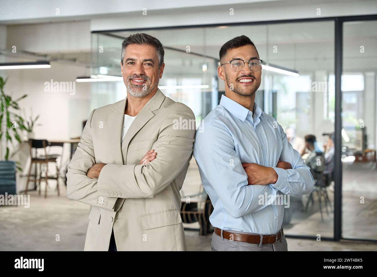 Two happy business partners standing back to back in corporate office ...