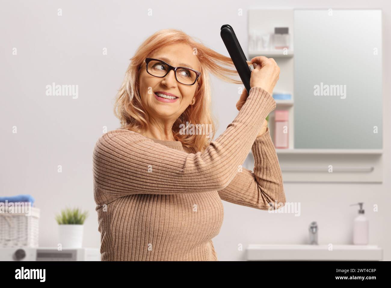 Middle aged woman using a wireless hair straightener in a bathroom ...