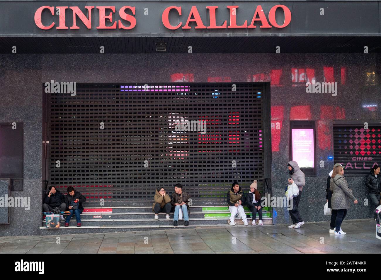 People sit outside a closed cinema theater, Cines Callao, in Madrid ...