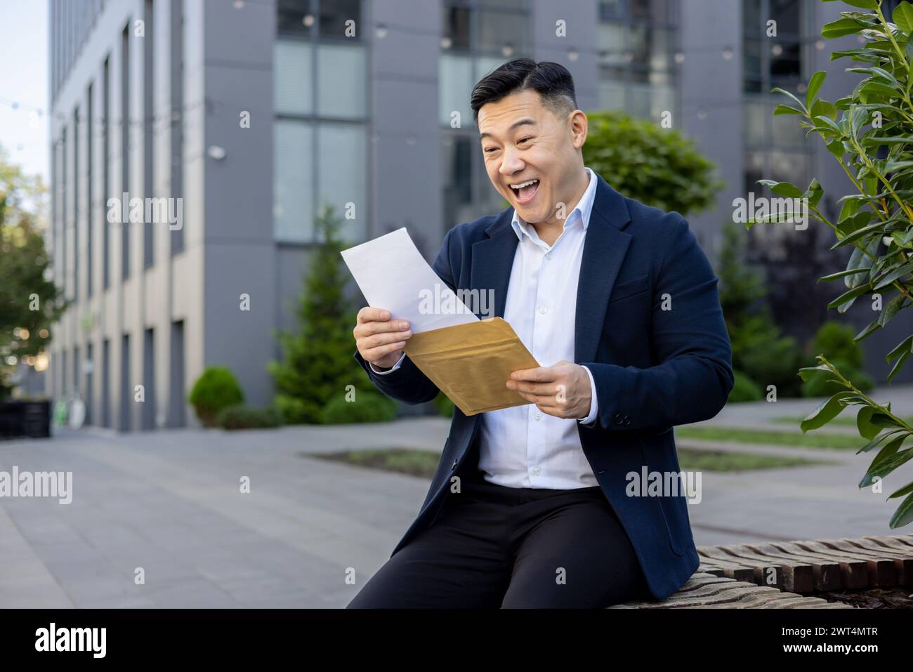 An ecstatic businessman in a suit sits outside an office building ...
