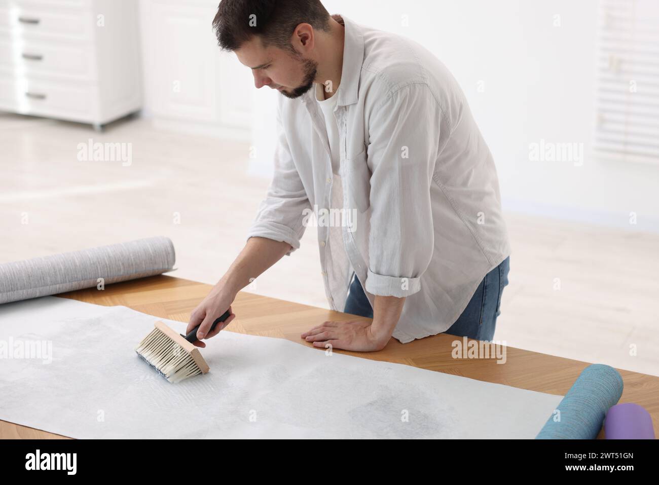 Man applying glue onto wallpaper sheet at wooden table indoors Stock ...