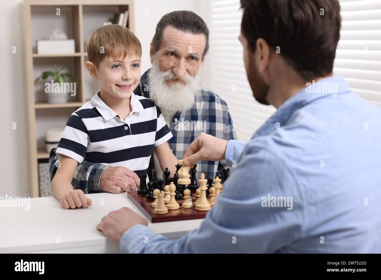 Family playing chess together at table in room Stock Photo - Alamy