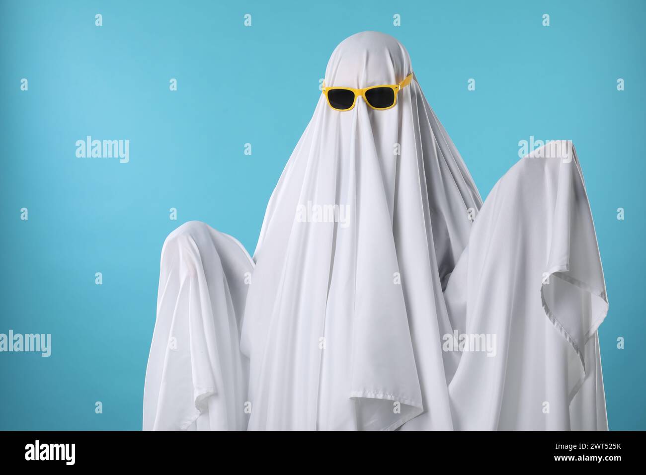 Stylish ghost. Person covered with white sheet in sunglasses on light ...