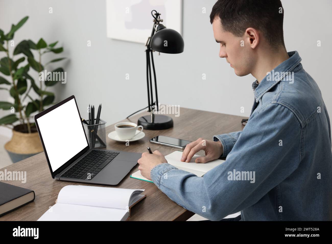 E-learning. Man taking notes during online lesson at table indoors ...