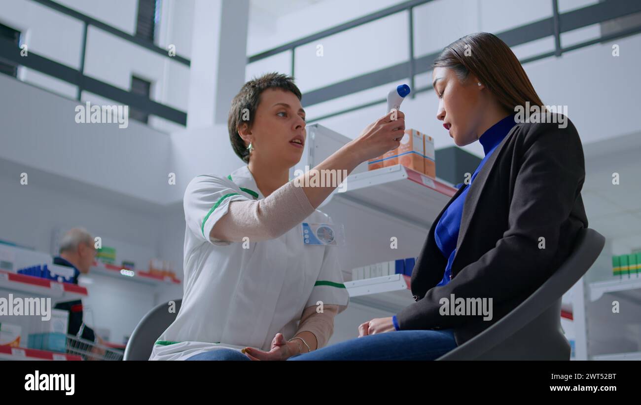 Pharmacist in drugstore using electronic thermometer on asian woman ...