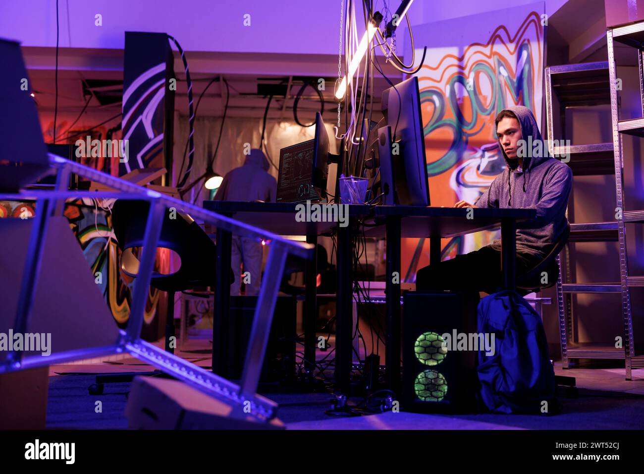 Asian hacker coding computer virus to steal personal information in database. Young man in hood ...