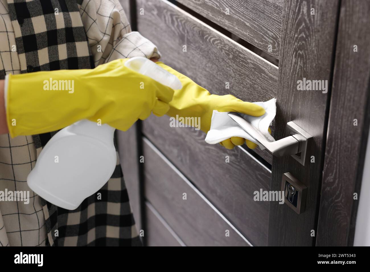 Woman cleaning door handle with detergent and paper towel, closeup ...