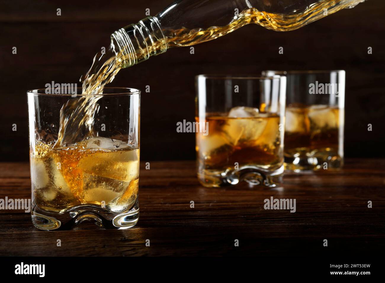 Pouring whiskey from bottle into glass at wooden table, closeup Stock ...