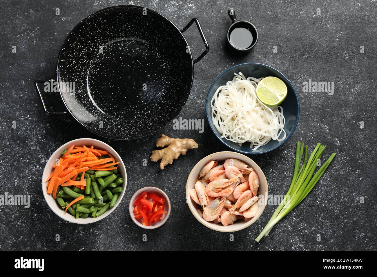 Flat lay composition with black wok and products on dark textured table ...