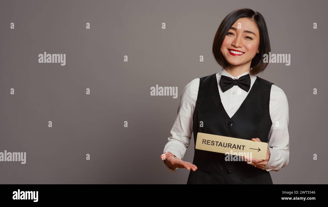 Asian hotel concierge holding restaurant sign to indicate direction ...