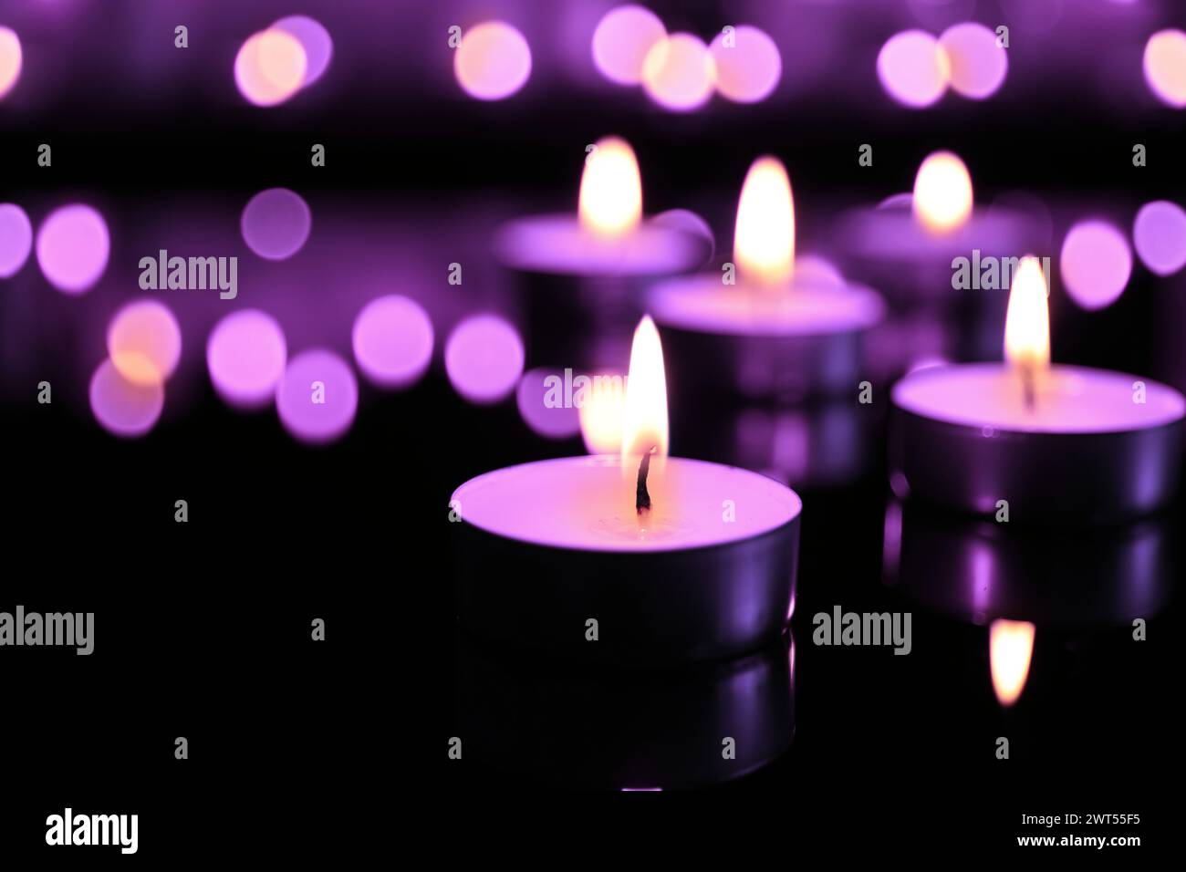 Burning violet candle on black background, closeup. Funeral attributes ...